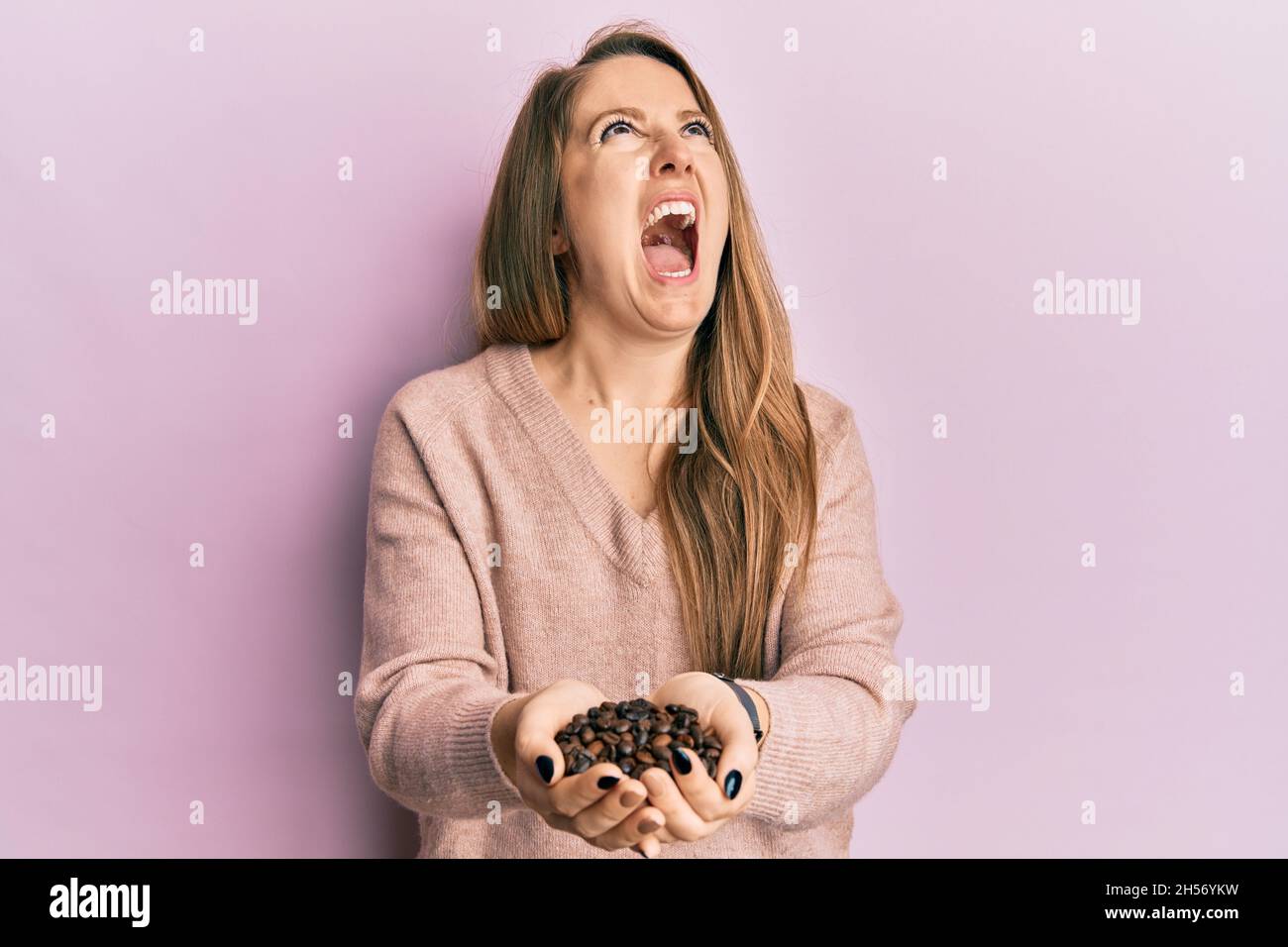 Young blonde woman holding coffee beans with hands angry and mad ...