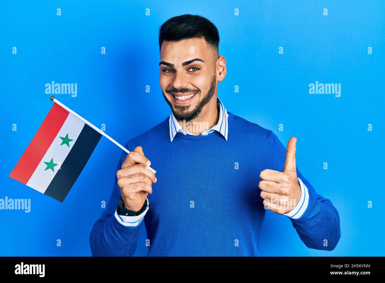 Young hispanic man with beard holding syria flag smiling happy and ...