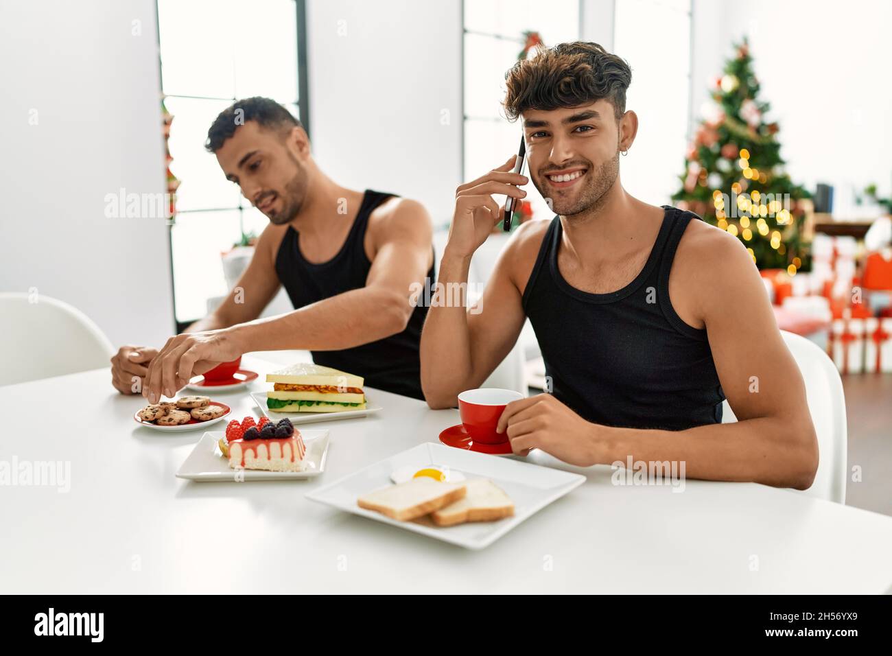 Two hispanic men couple having breakfast and talking on the smartphone ...