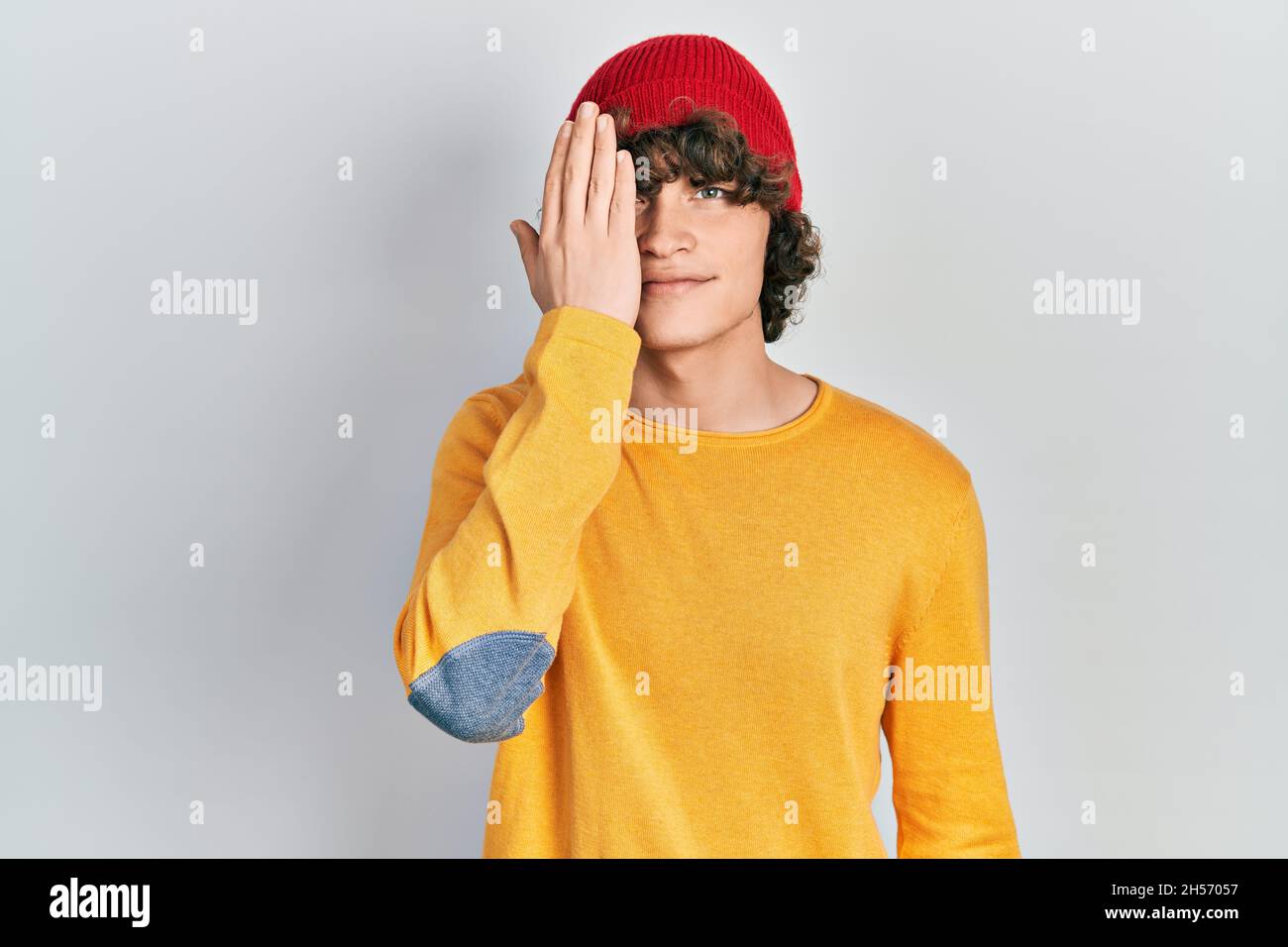 Handsome young man wearing wool hat covering one eye with hand ...