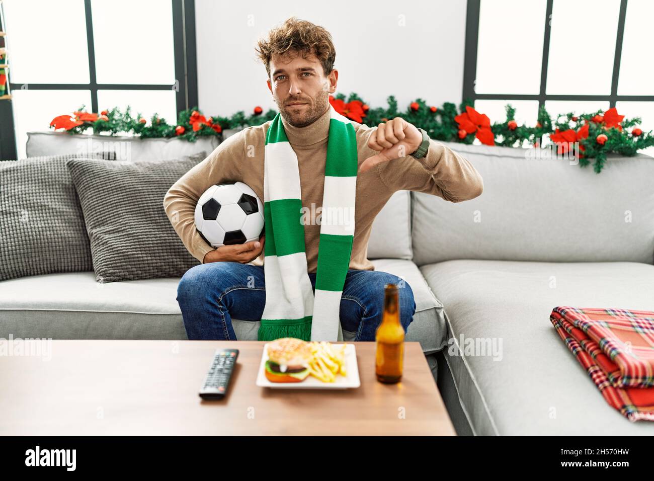 Young hispanic man football hooligan holding ball at home with angry ...