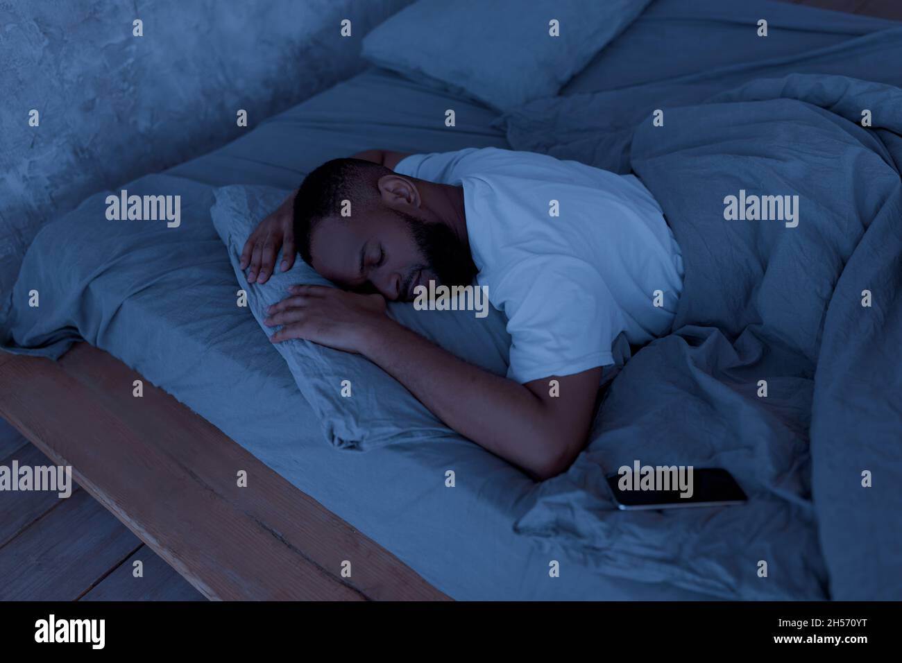 Young African American man sleeping in bed with cellphone Stock Photo ...