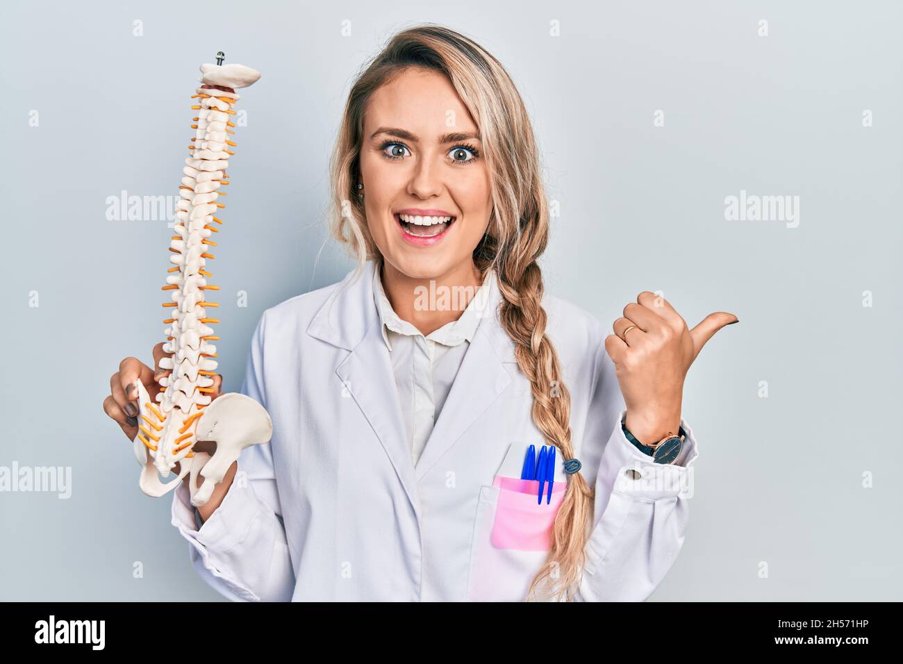 Beautiful young blonde doctor woman holding anatomical model of spinal ...