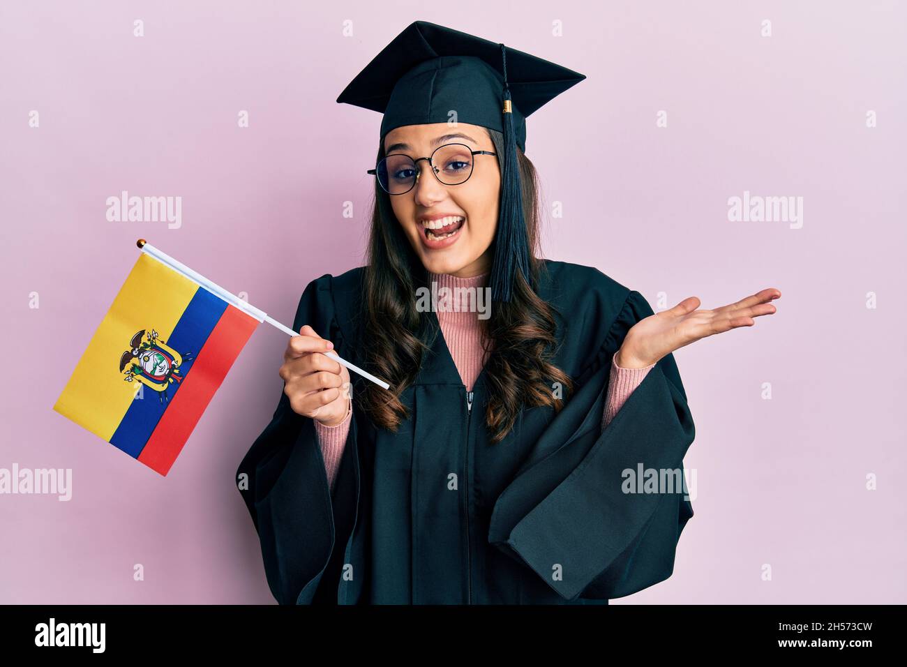Young hispanic woman wearing graduation uniform holding ecuador flag ...
