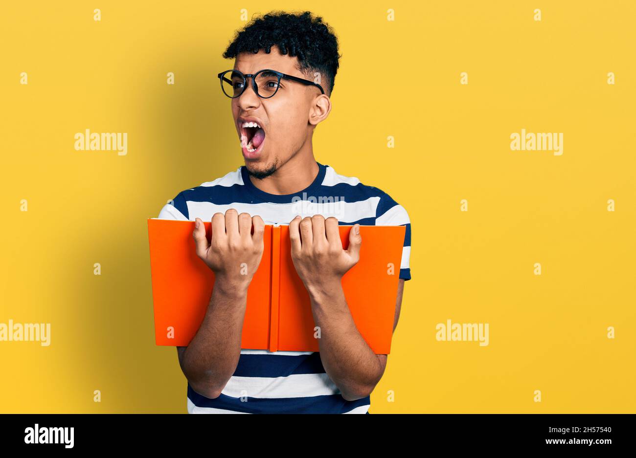 Young african american man reading a book with glasses angry and mad ...