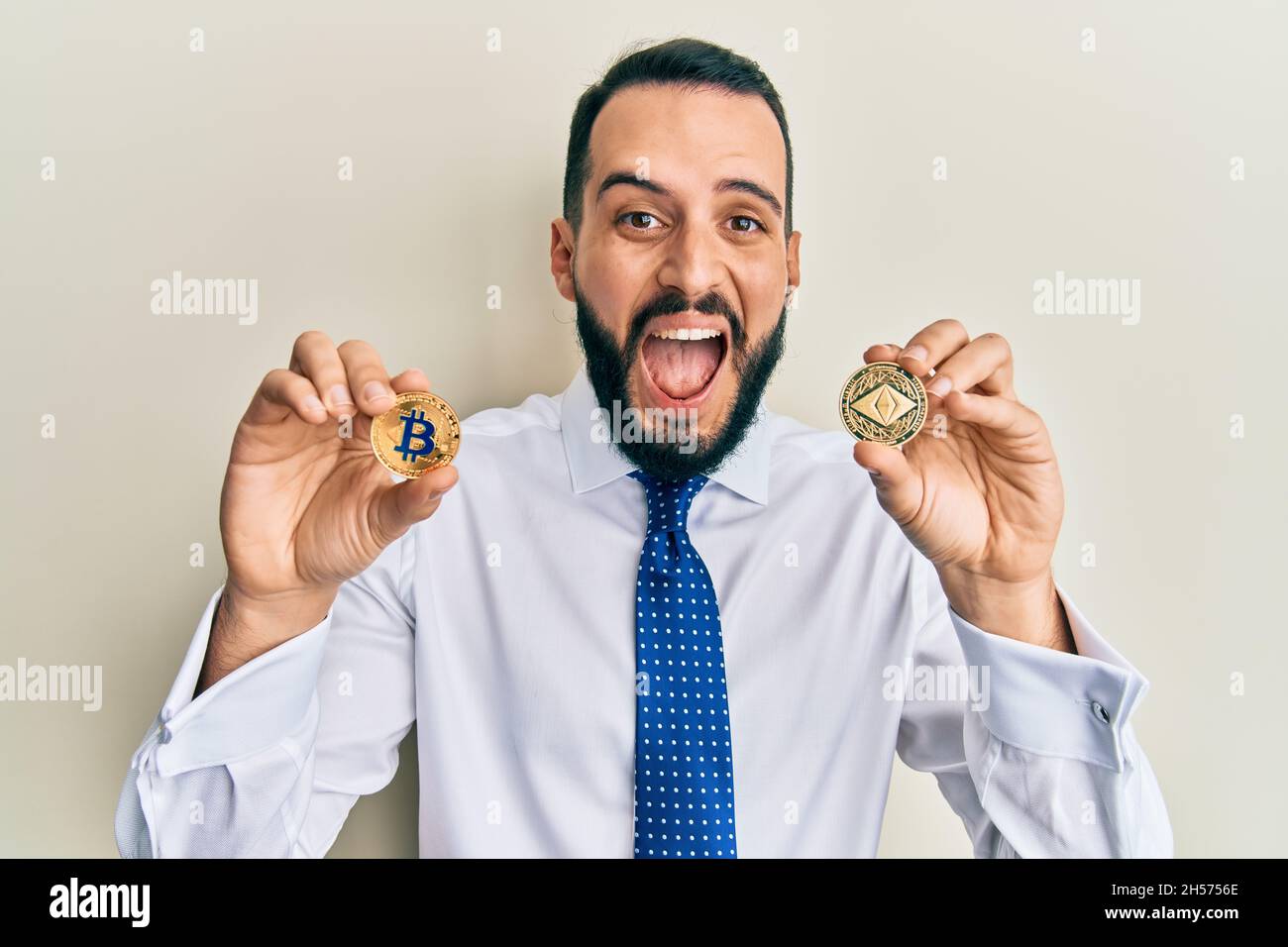 Young man with beard holding virtual currency ethereum coin and bitcoin ...