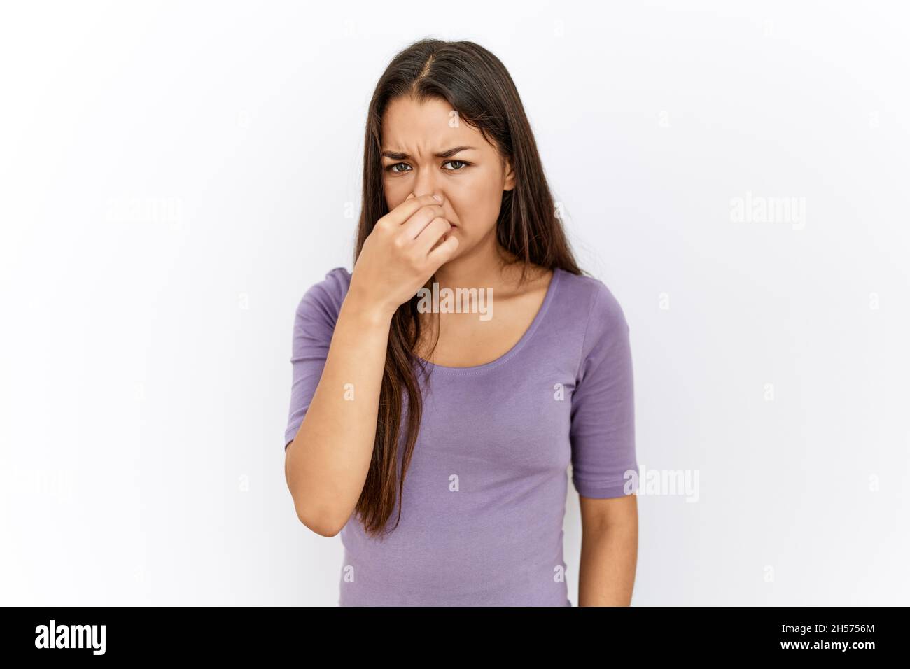 Young brunette woman standing by isolated background smelling something ...