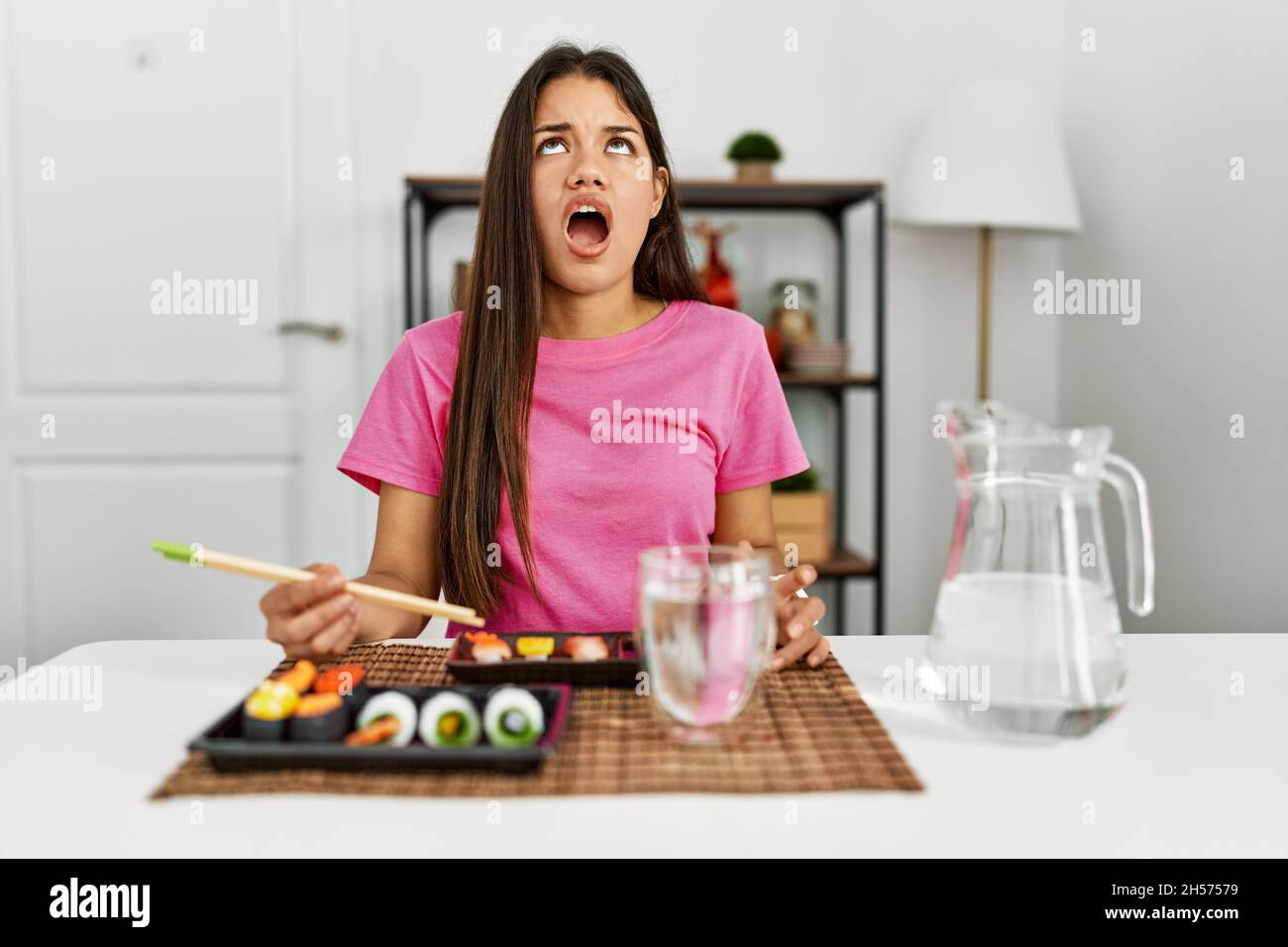 Young brunette woman eating sushi using chopsticks angry and mad ...