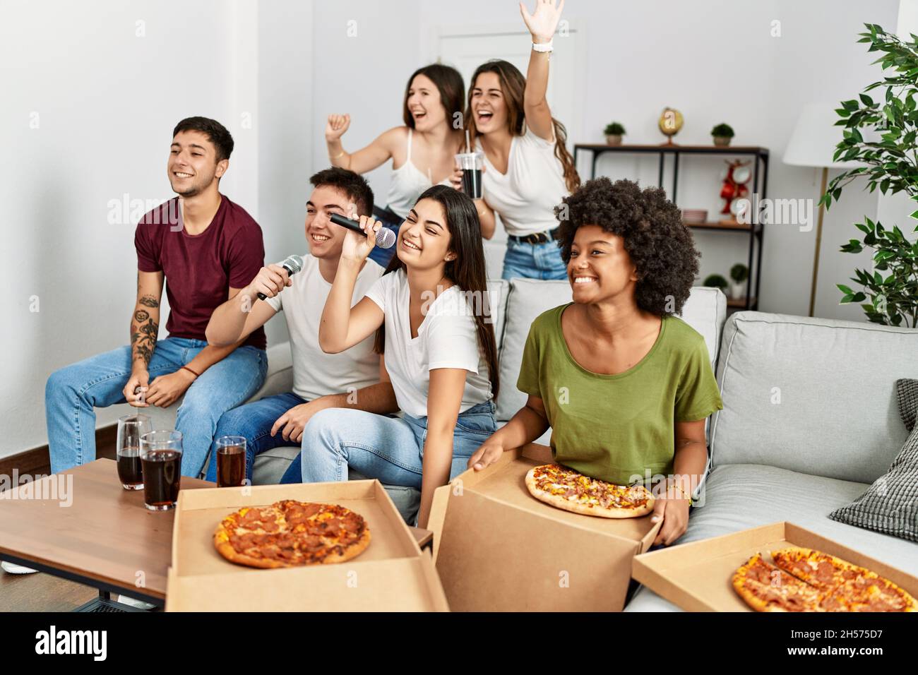Group of young friends having party eating italian pizza and singing ...