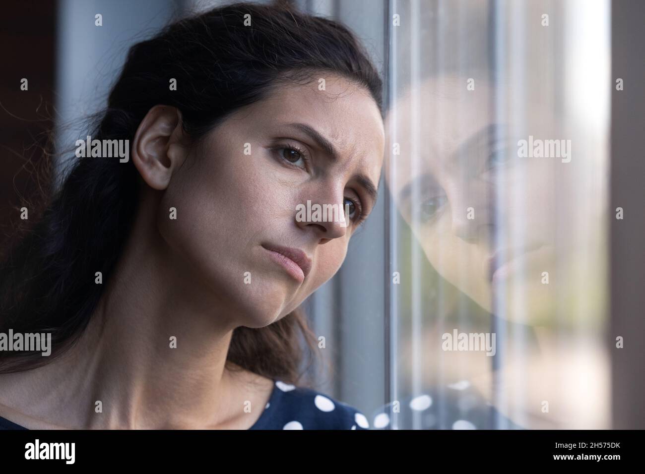Sad millennial female pressing forehead against window suffer of ...
