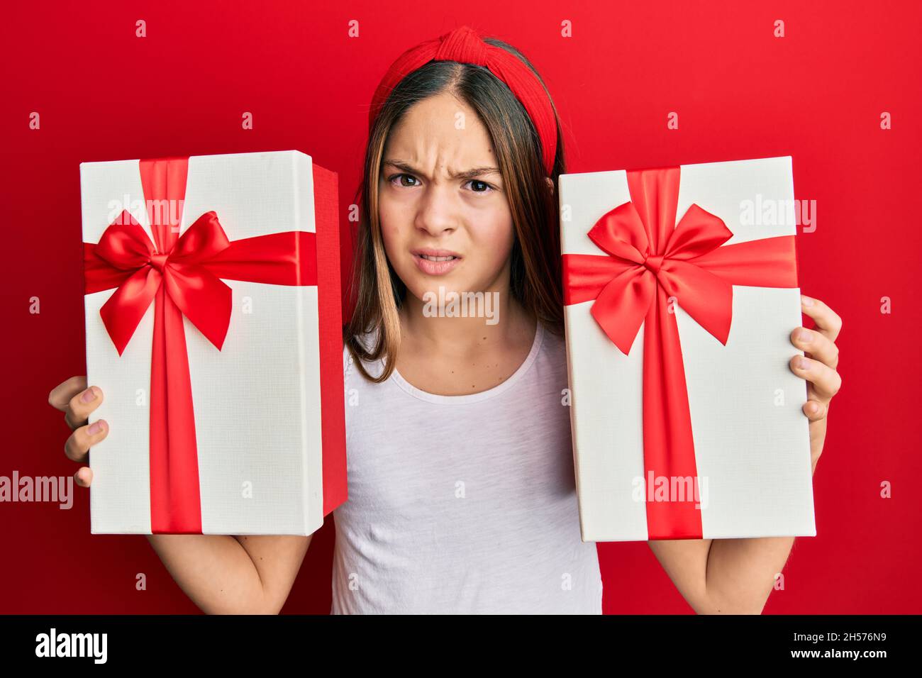 Beautiful brunette little girl holding gifts clueless and confused ...