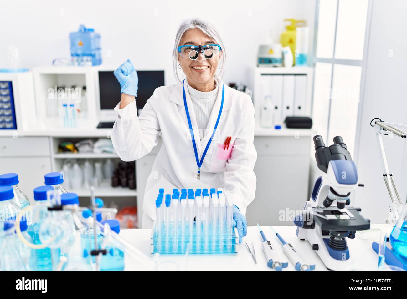 Middle age grey-haired woman wearing scientist uniform screaming proud ...