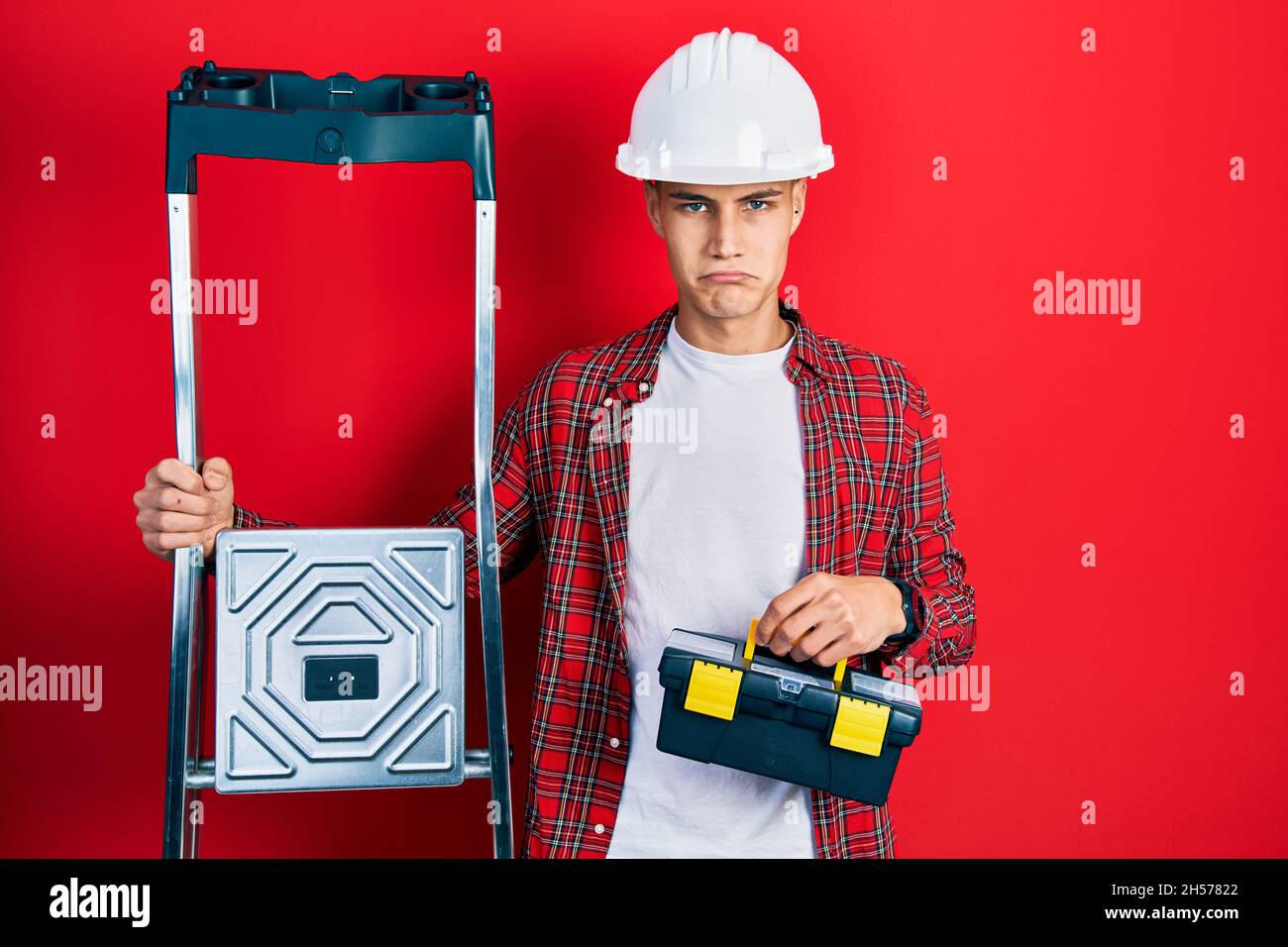 Young hispanic man holding tools box wearing hardhat by construction ...