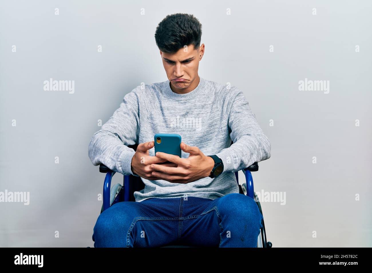 Young hispanic man sitting on wheelchair using smartphone depressed and ...