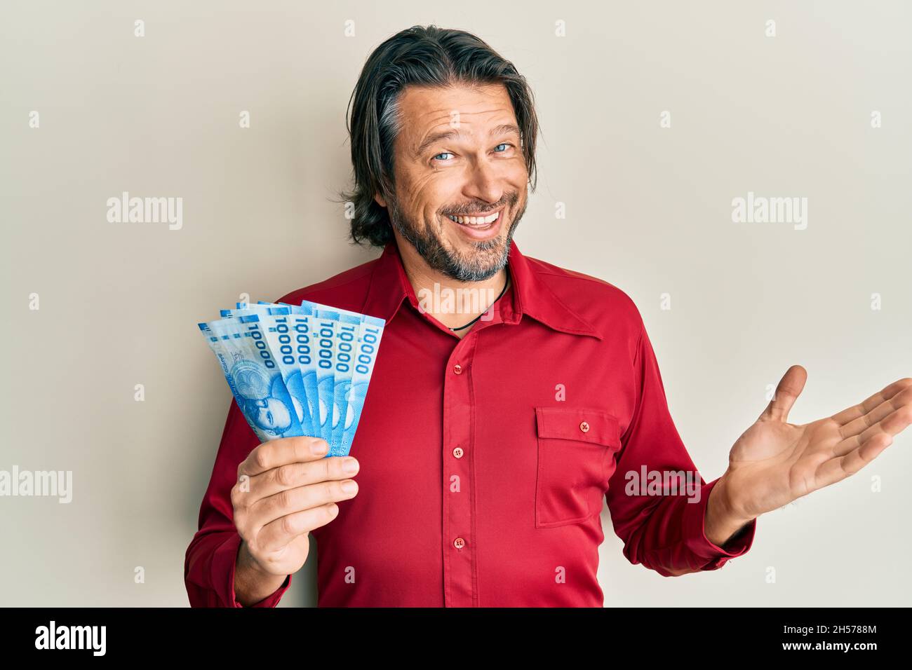 Middle age handsome man holding 10000 chilean pesos celebrating ...