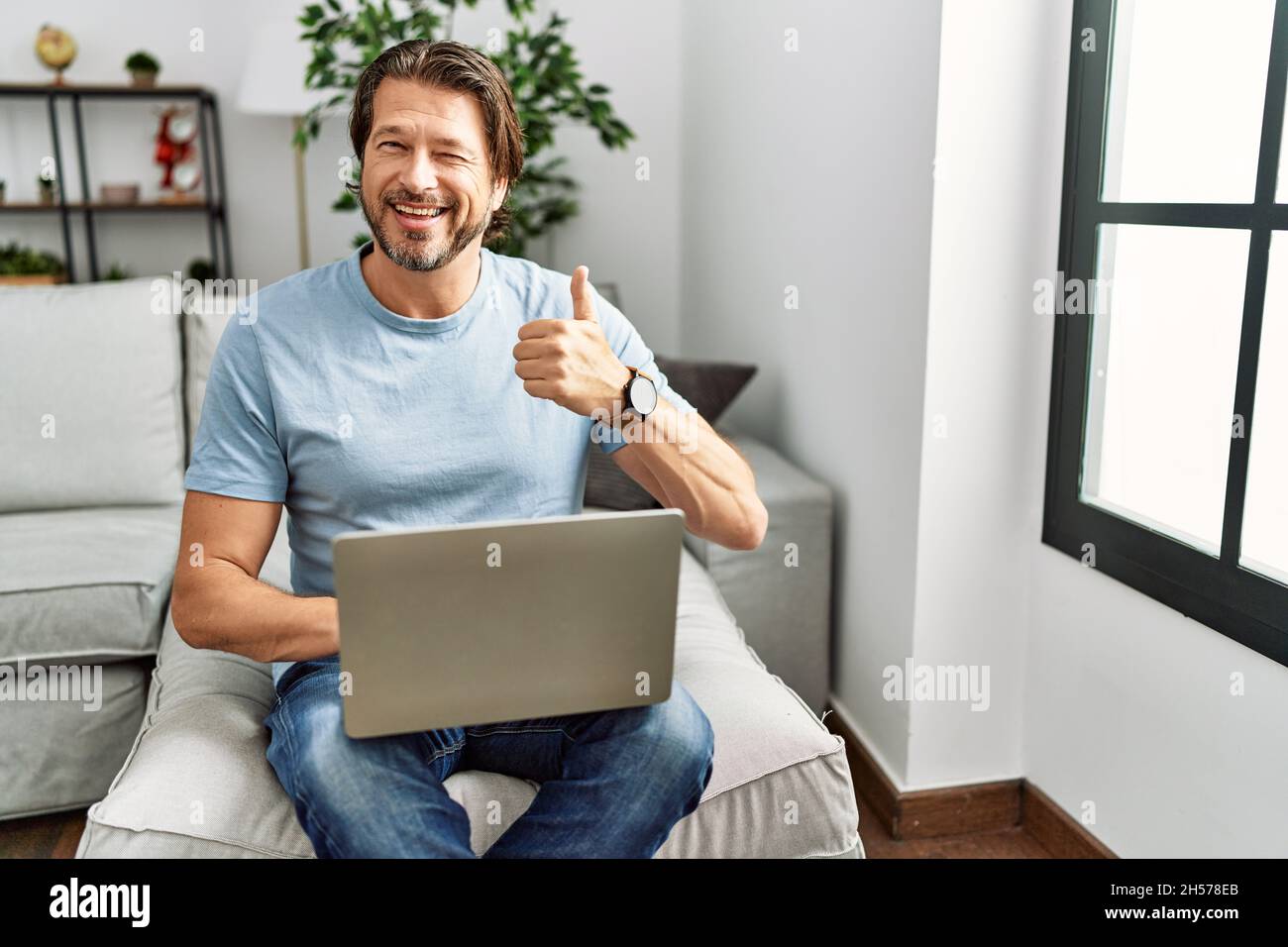 Handsome middle age man using computer laptop on the sofa doing happy ...