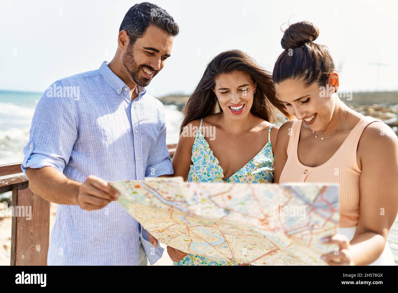 Three young hispanic friends smiling happy searching route on city map ...