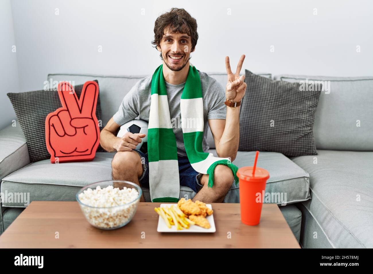 Young hispanic man football hooligan cheering game at home smiling with ...