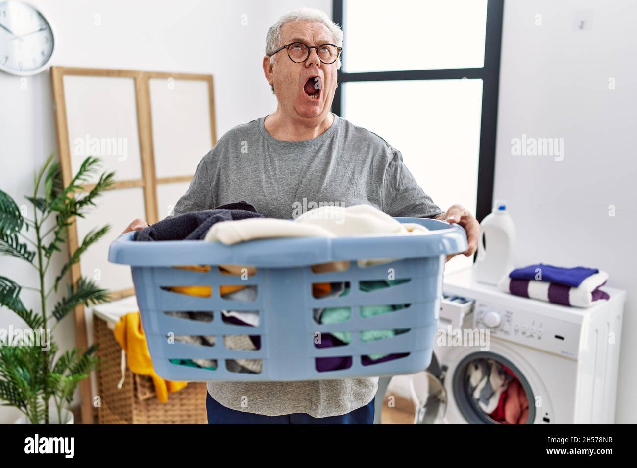 Senior caucasian man holding detergent bottle at laundry room angry and ...