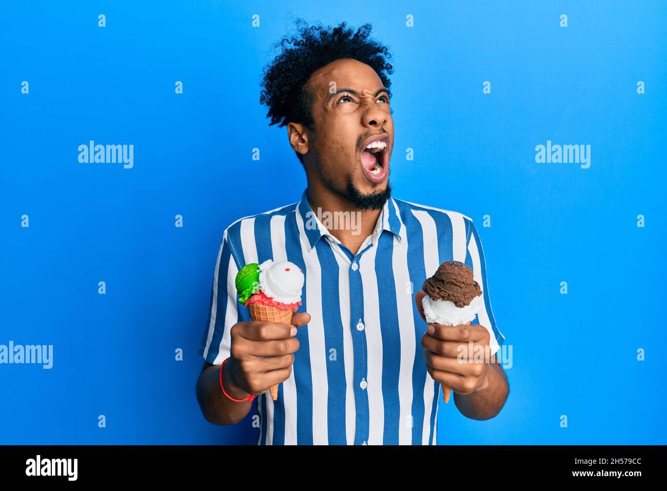 Young african american man with beard holding two ice cream cones angry ...