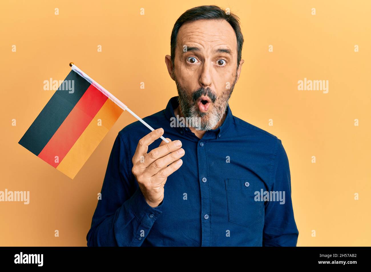 Middle age hispanic man holding germany flag scared and amazed with ...