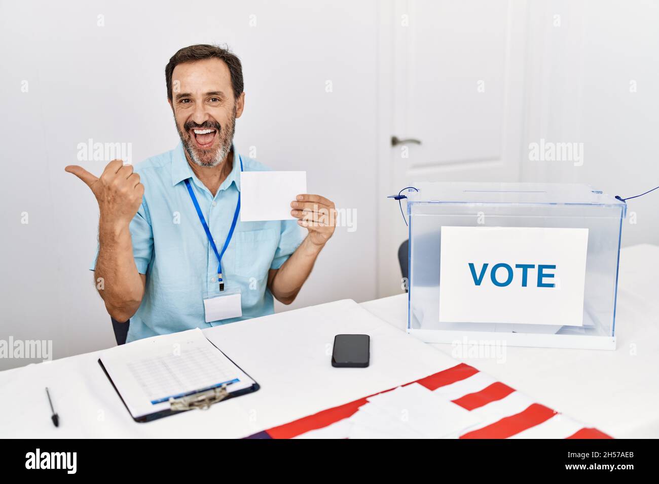 Middle age man with beard voting putting envelop in ballot box pointing ...