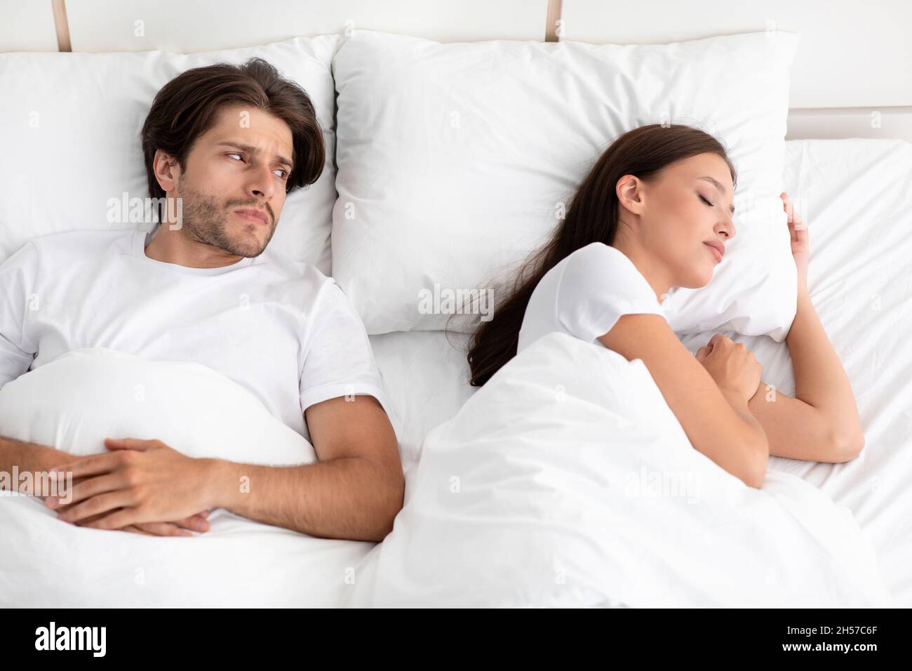 Disgruntled sad caucasian young guy does not sleep, lies in bed, looks ...