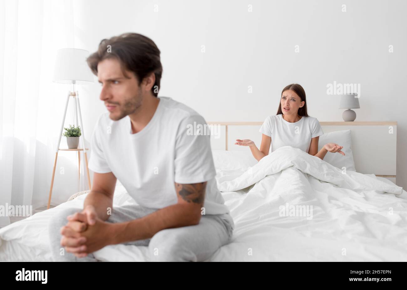 Upset Offended Young European Man Sitting On Bed Ignoring Lady Wife