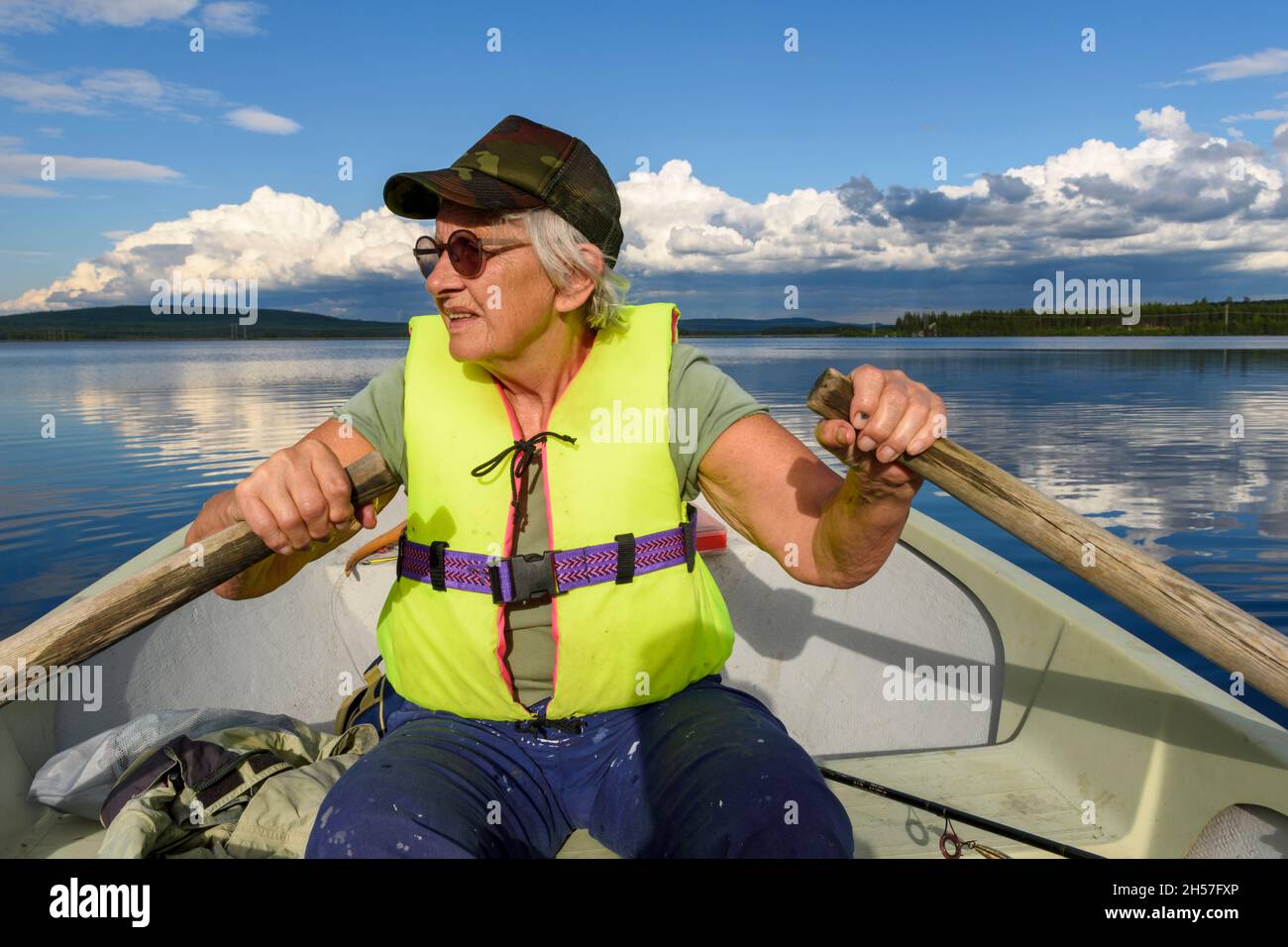 Woman rowing a little rowboat on a calm lake with a blue sky and some ...