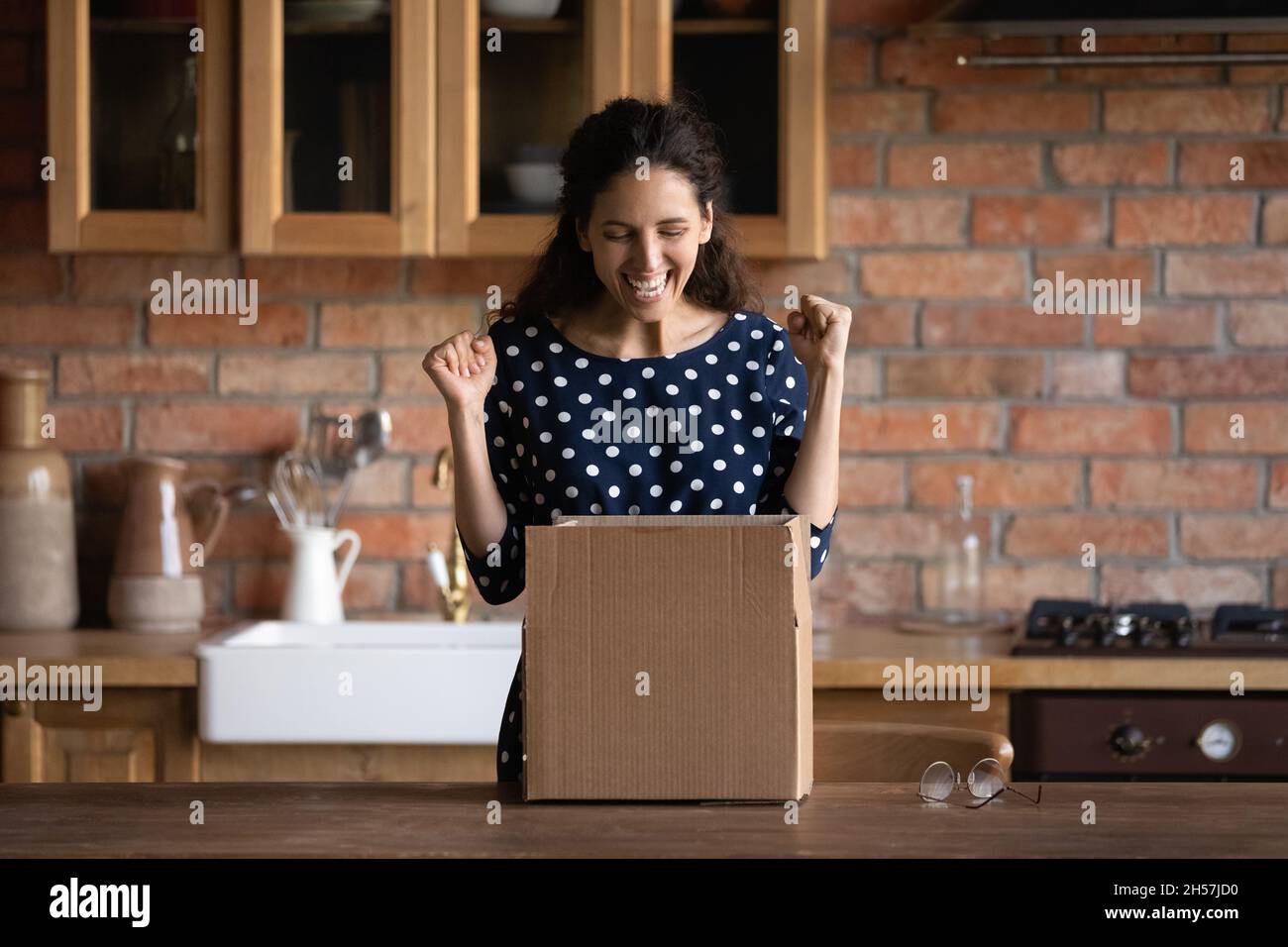 Overjoyed latin female customer open delivery box at kitchen table ...