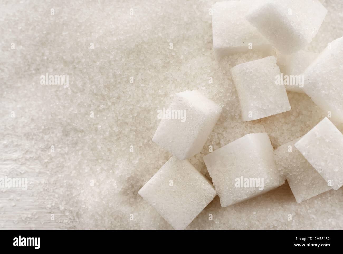 Refined sugar cubes are scattered over loose sugar. Sucrose ingredient ...