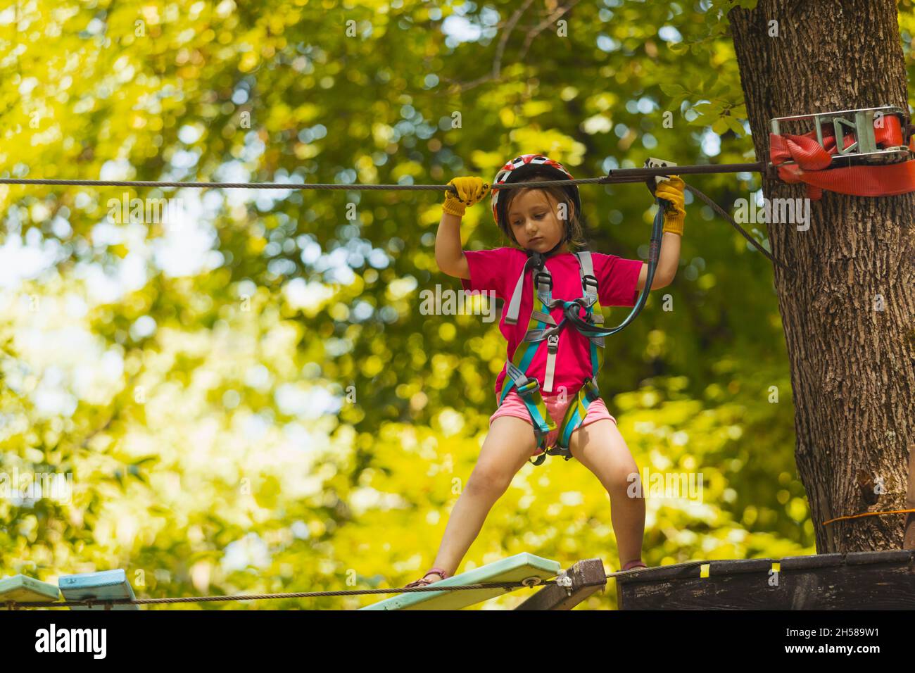 The concentrated girl carefully overcomes obstacles in the rope park ...