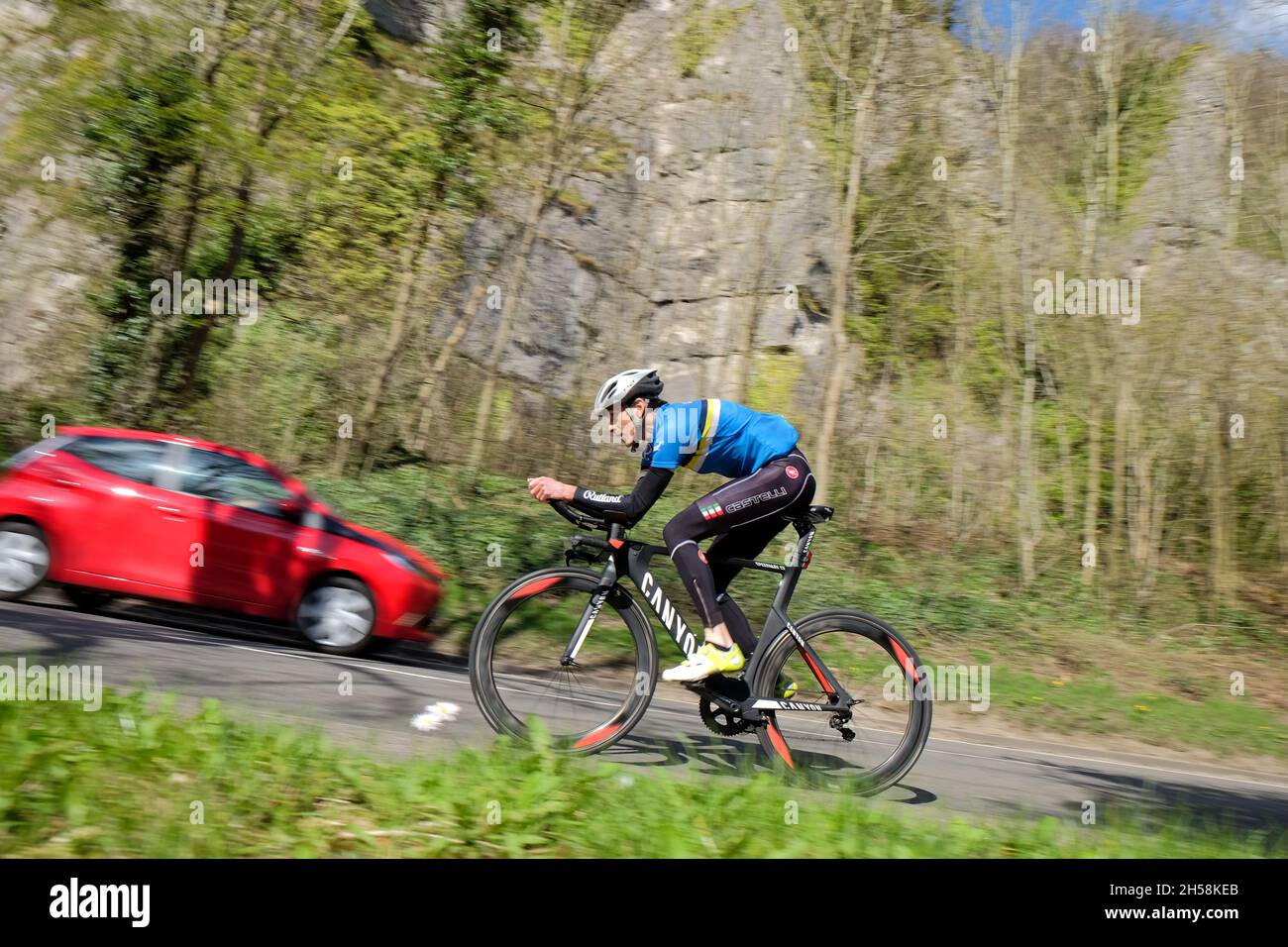 Cyclists riding up hill with stoney crags behind on the A623 in the ...