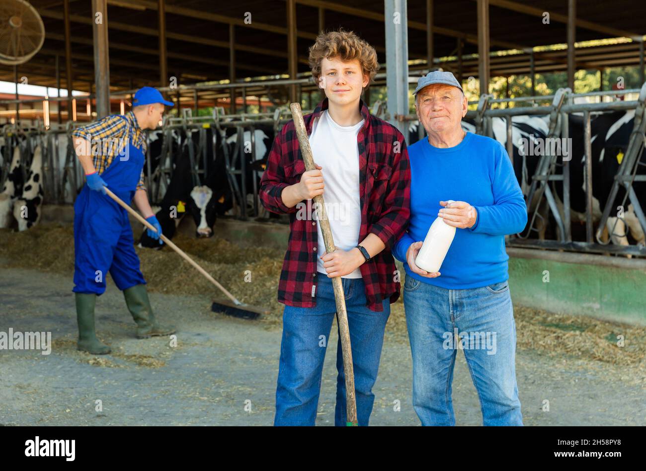Portrait of an elderly farmer and his young assistant with bottle of ...