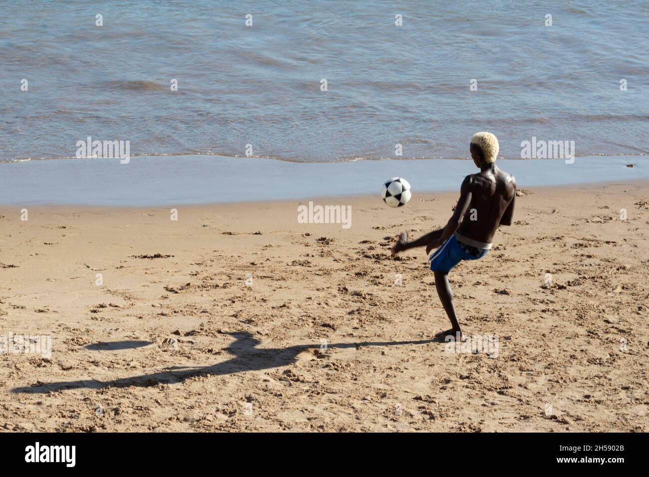 Young model playing sand football on the beach under strong summer sun ...