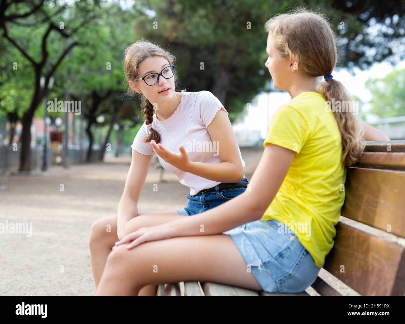 Two girls sitting on bench in park and laughing Stock Photo - Alamy