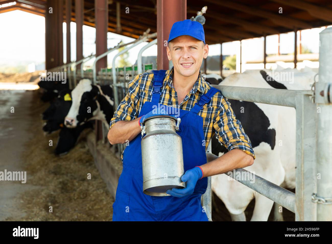 Portrait of positive dairy farm worker in blue overalls with can of ...