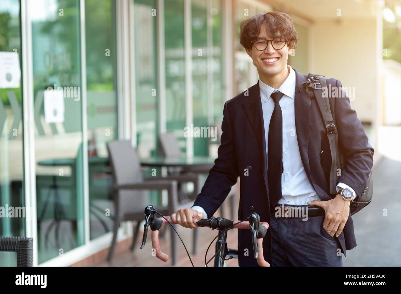 Confident handsome asian young businessman going to work by bike, walking outdoors with a ...