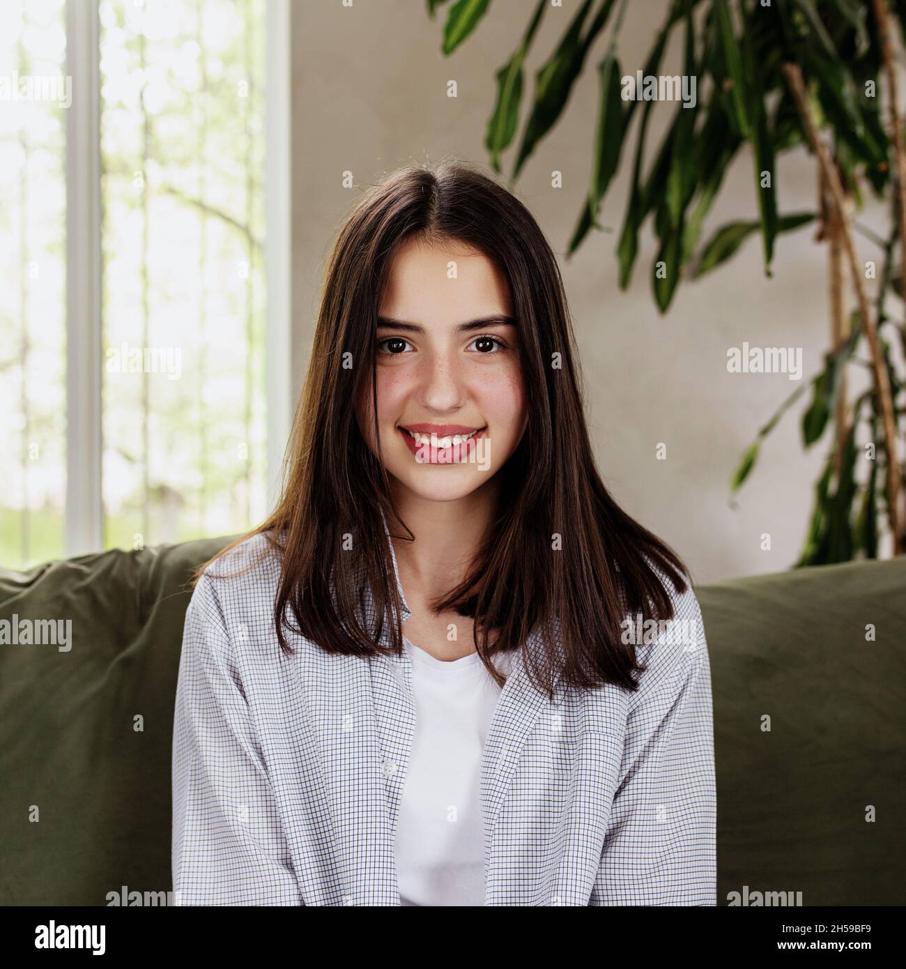 Beautiful smiling caucasian girl sitting at green sofa and watching at ...