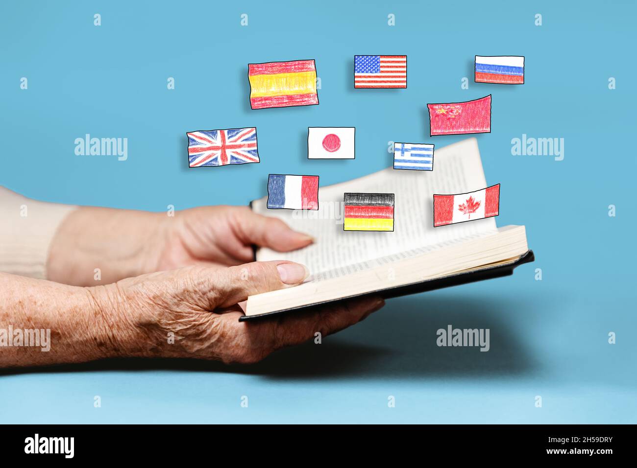 Education. A senior woman reading a book with flags of different ...
