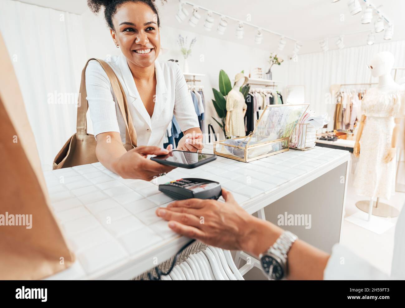 Happy customer paying through smartphone at a counter in a clothing ...