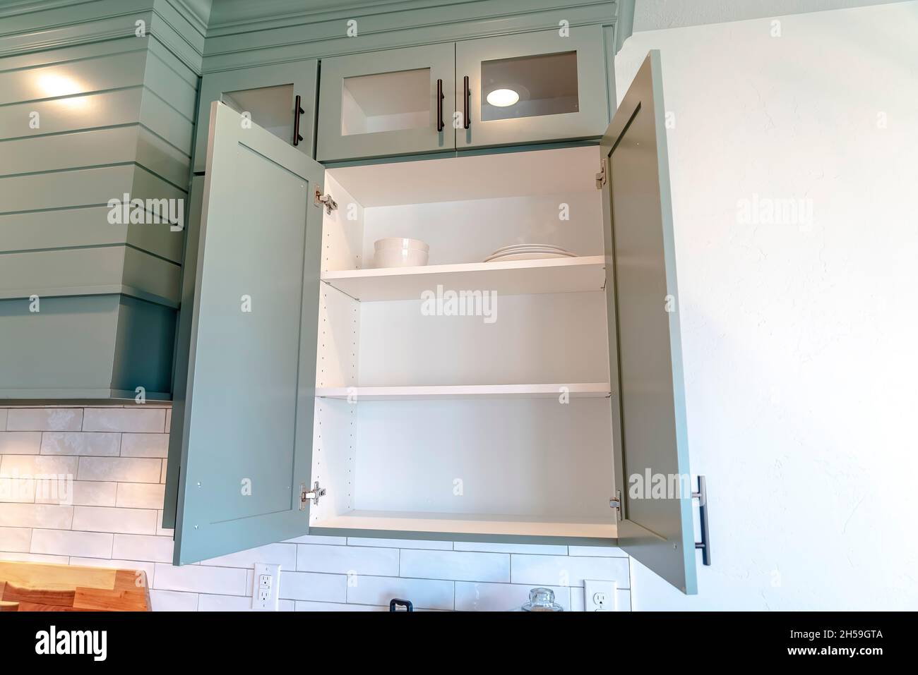 Wall cabinet with open door over white tile backsplash inside kitchen ...