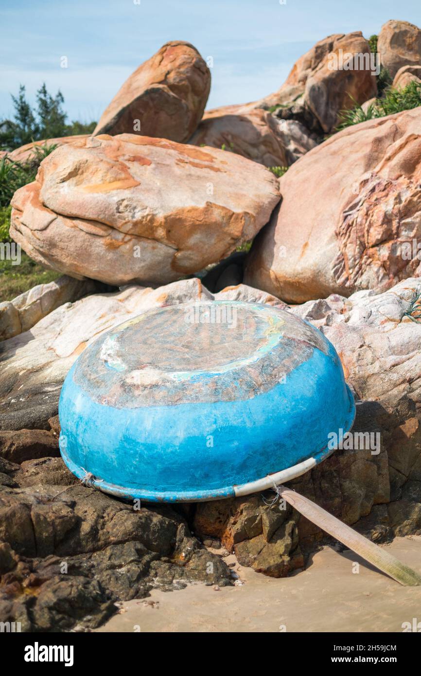 Round blue Vietnamese fishing boat lies upside down on large rocks on ...