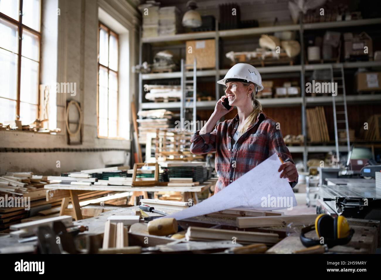 Female engineer holding blueprints and making phone call indoors in ...