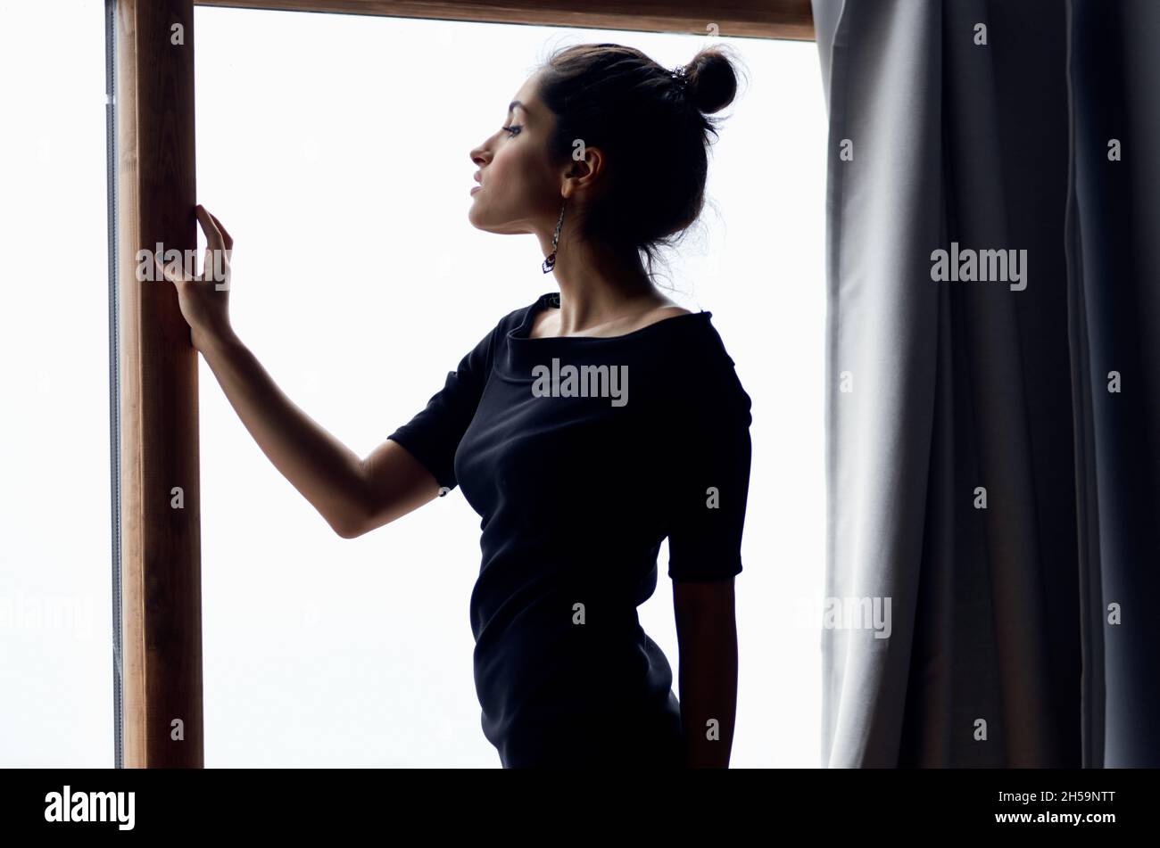 beautiful woman in a black dress near the window posing elegant style ...