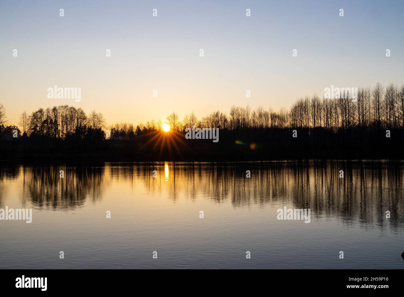 Beautiful sunset landscape, sun over water surface and treetops ...