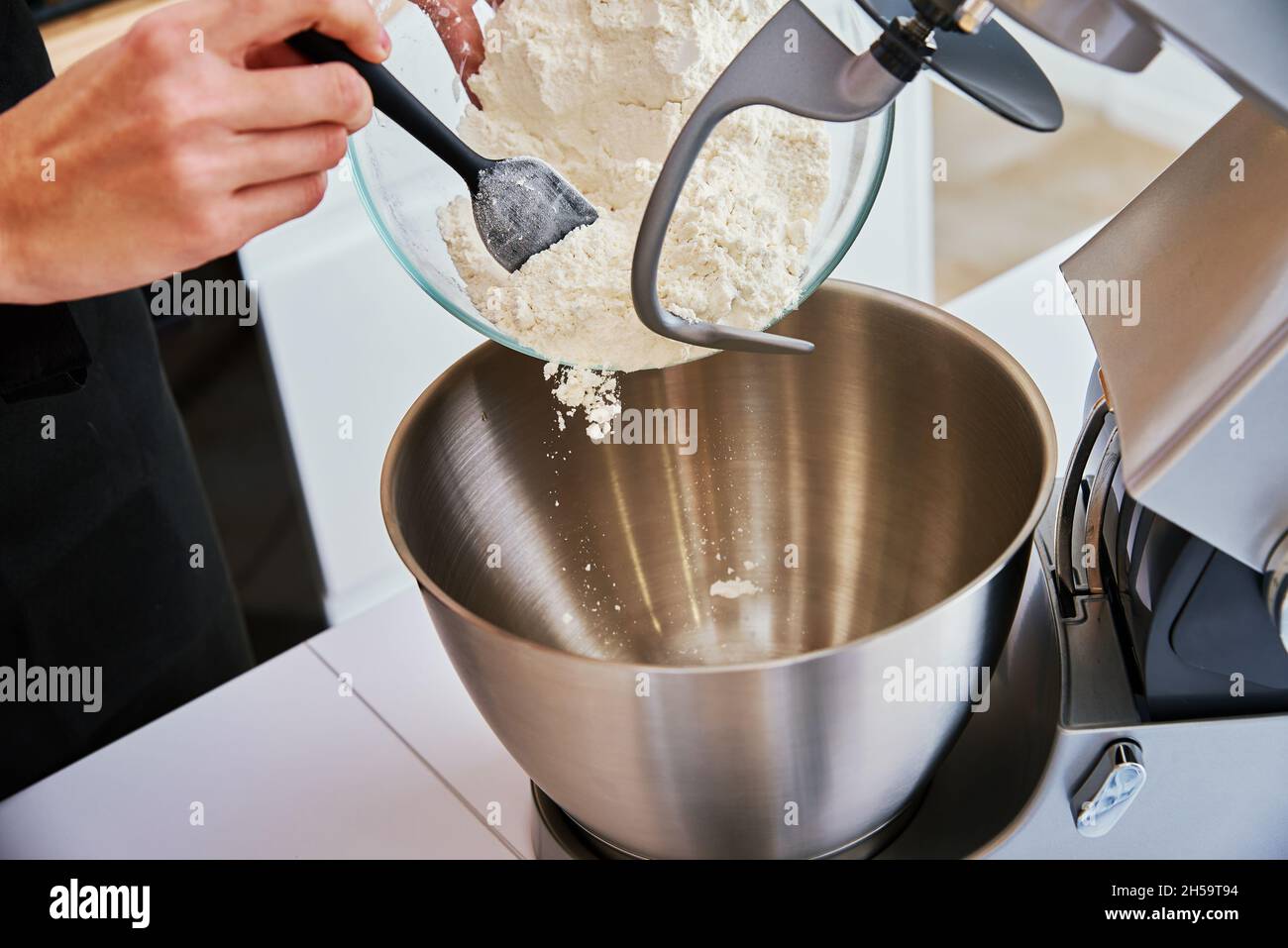 Woman prepares dough using kitchen mixer, pouring ingredients into ...