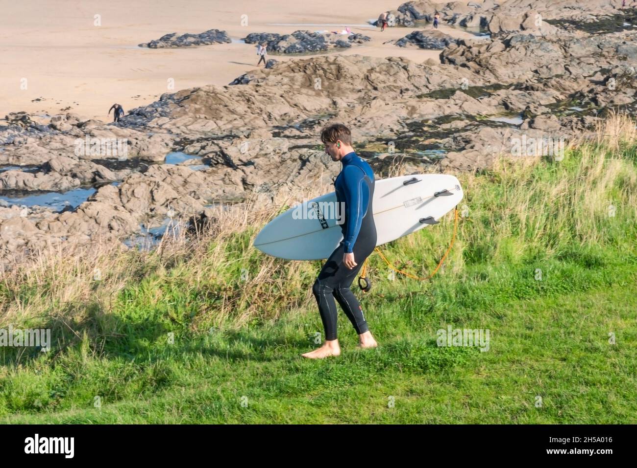 A surfer carrying his surfboard walking down a footpath to Fistral ...