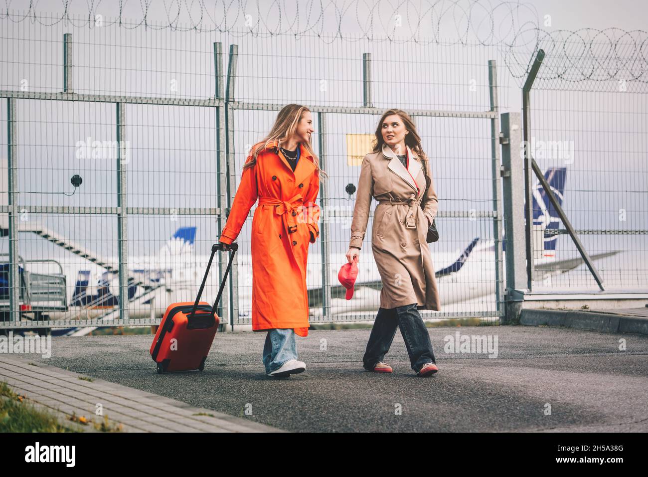 Two happy girls walking near airport, with luggage. Air travel, summer ...