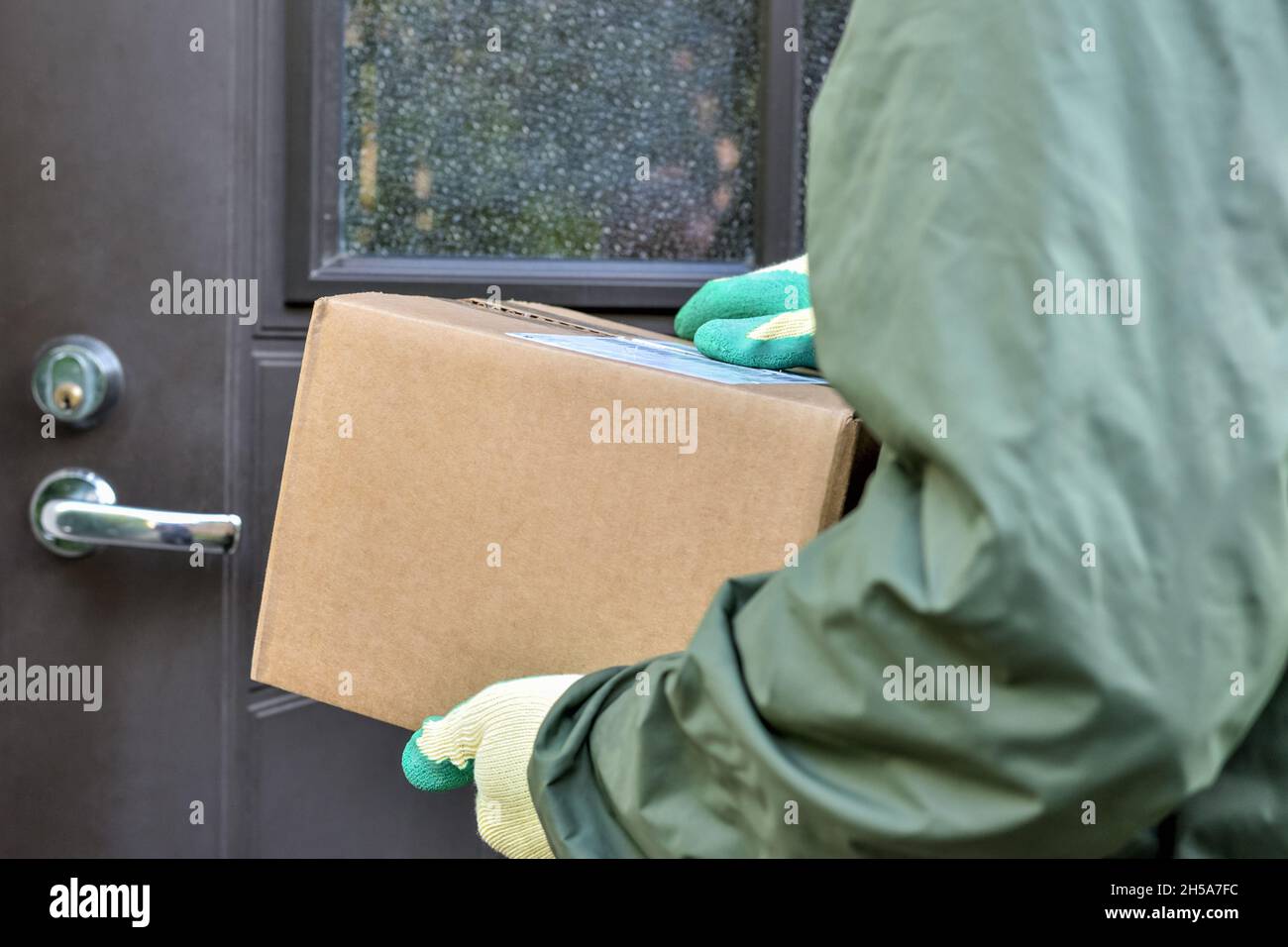 Cardboard box in the hands of the postman on the background of the door ...